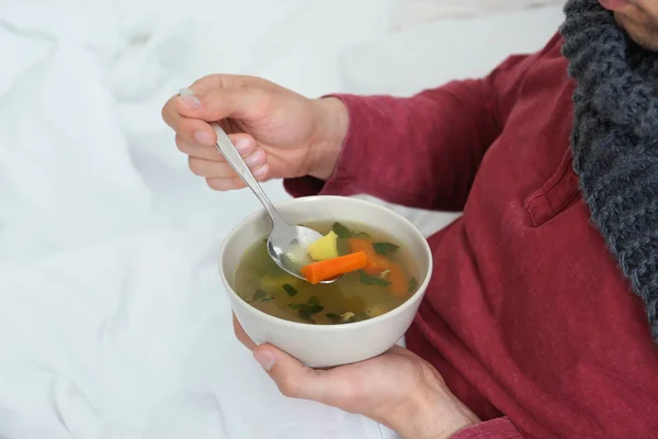 Sick young man eating broth to cure cold in bed at home - Stock Image ...