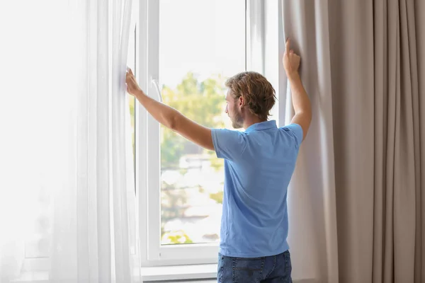 Smiling man opening window Stock Photo by ©belchonock 157996778