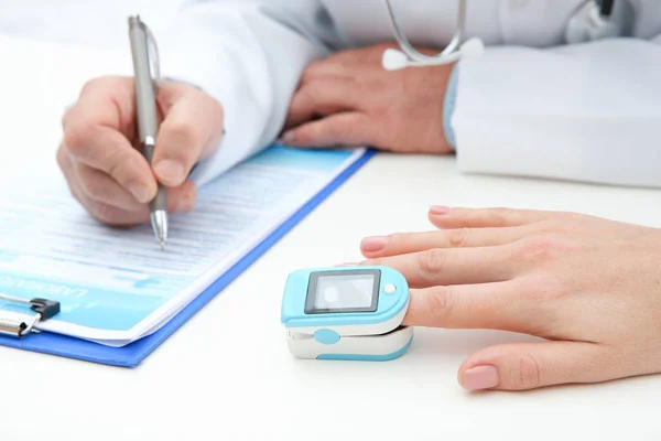 Doctor checking young woman's pulse with medical device at table in ...