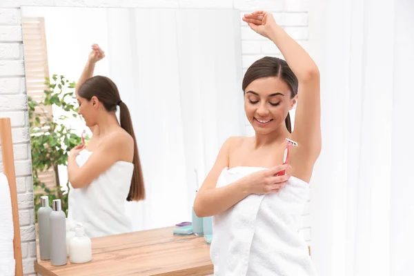 Beautiful young woman shaving armpit at home - Stock Image - Everypixel