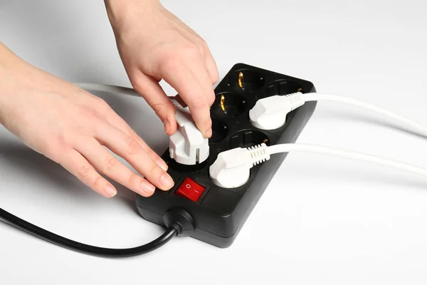 Woman pressing power button of extension cord on white background ...