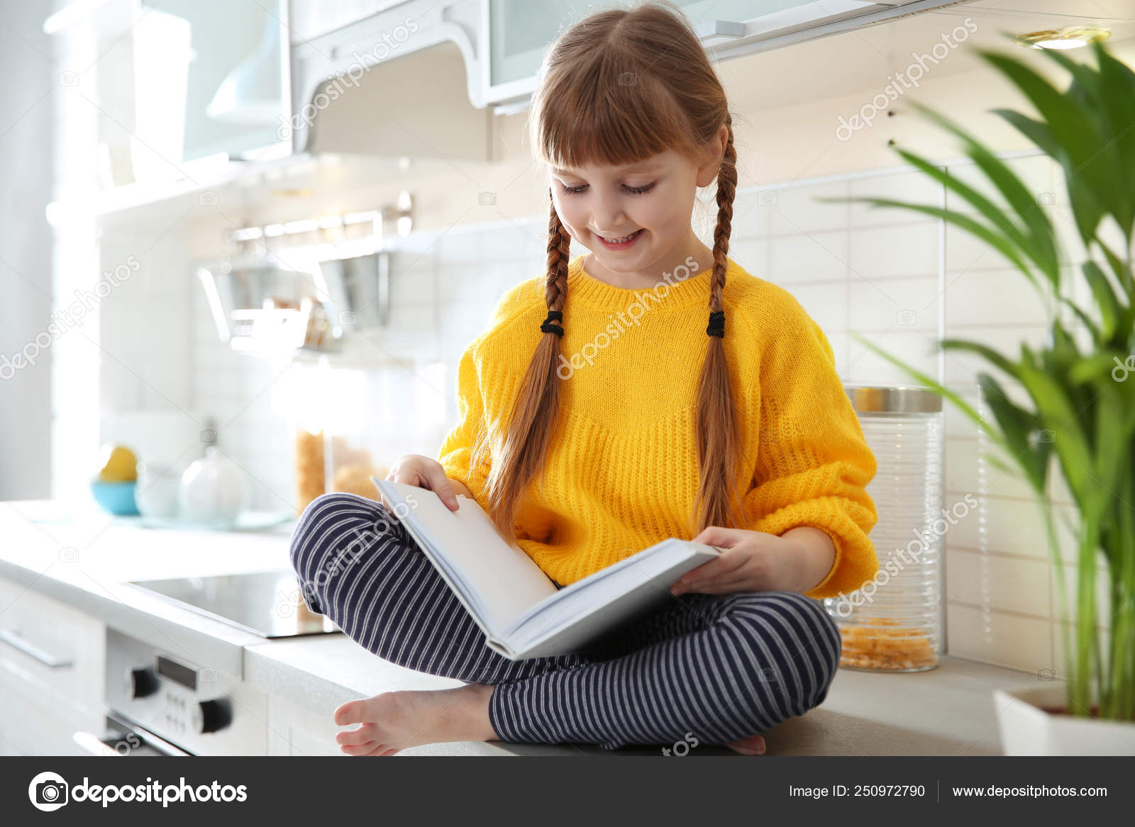 Cute little girl reading book in kitchen at home Stock Photo by ...