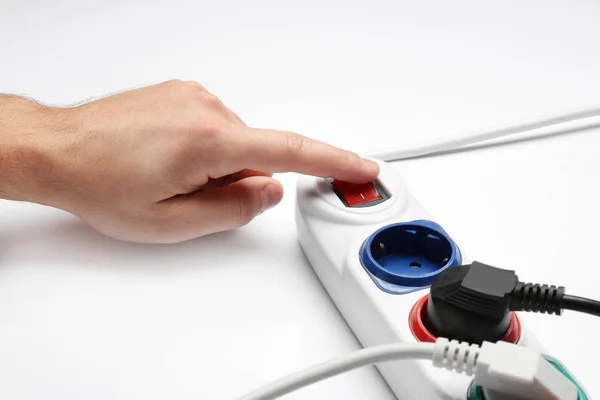 Woman pressing power button of extension cord on white background ...