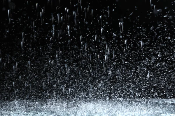 Heavy rain falling down on ground against dark background, closeup ...