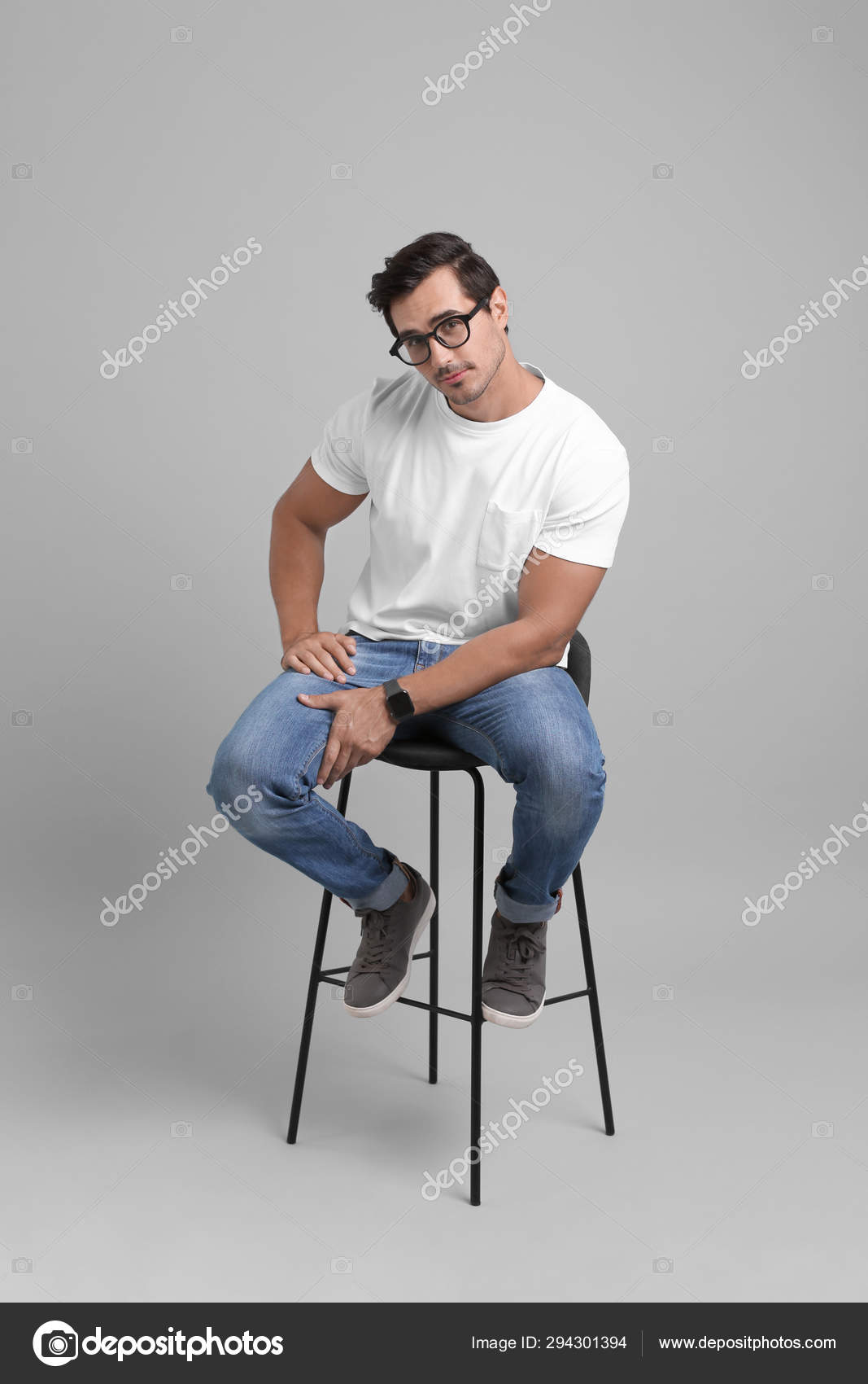 Handsome young man sitting on stool against grey background Stock Photo ...