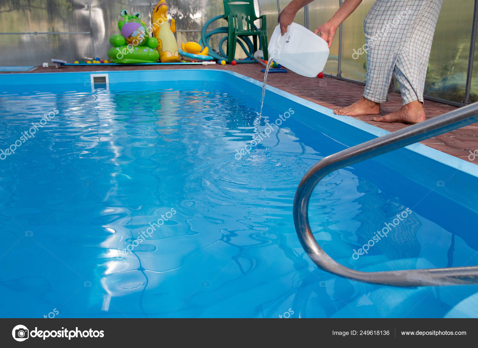 Men's hands pour light liquid from a plastic tank into a pool, into ...