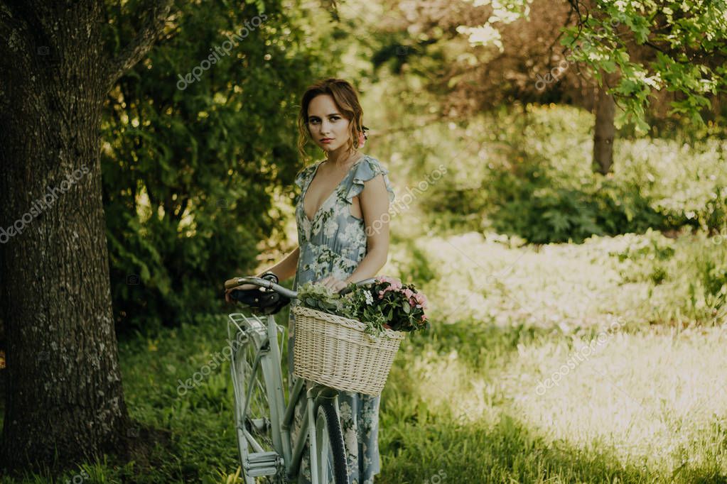 retrato de una hermosa niña en el bosque, sosteniendo una bicicleta con una cesta de flores ...