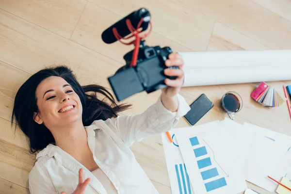 Mirthful friendly lady making a lifestyle blog and smiling while lying ...