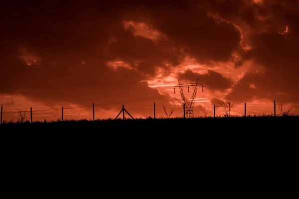 Scary sunset, with red sky and clouds, after the storm. Power pylons ...