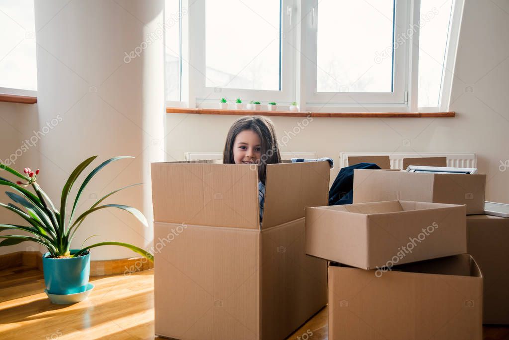 feliz niño hija en caja emocionado acerca de mover día o reubicación, alegre chica jugando ...