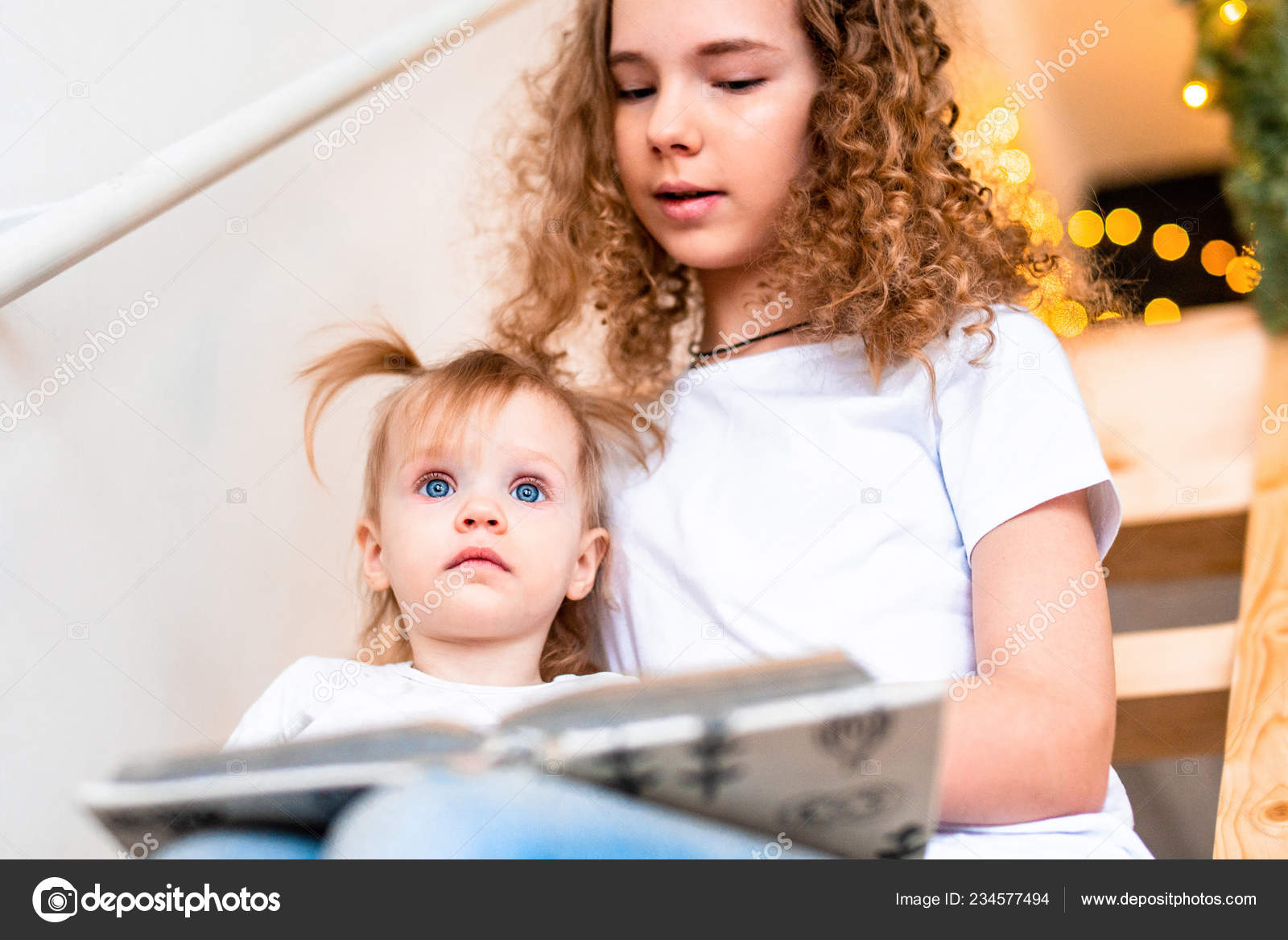 Elder sister reading book aloud to her younger sister at staircase ...