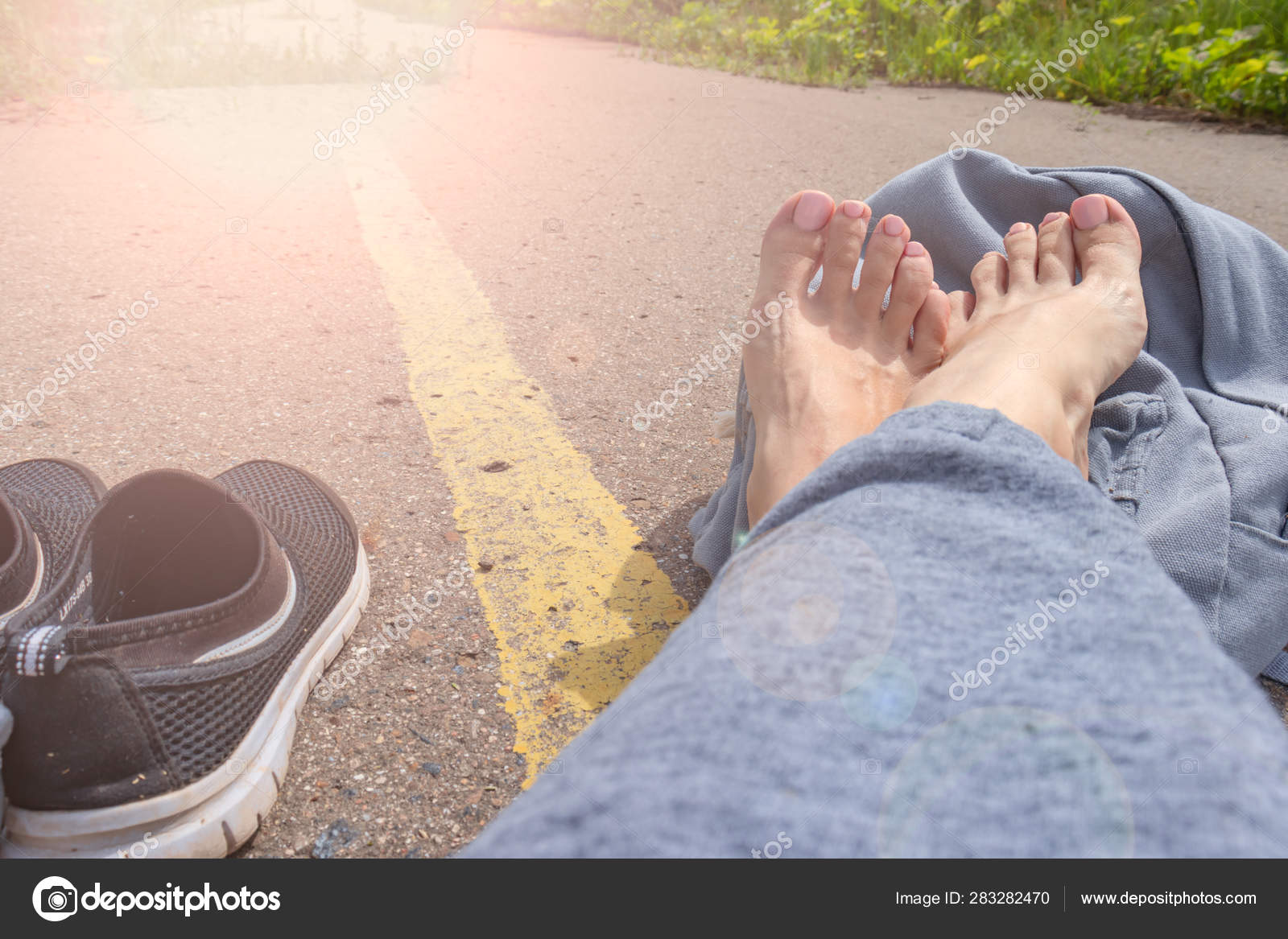 Woman with bare feet and backpack sitting on an asphalt road with a ...