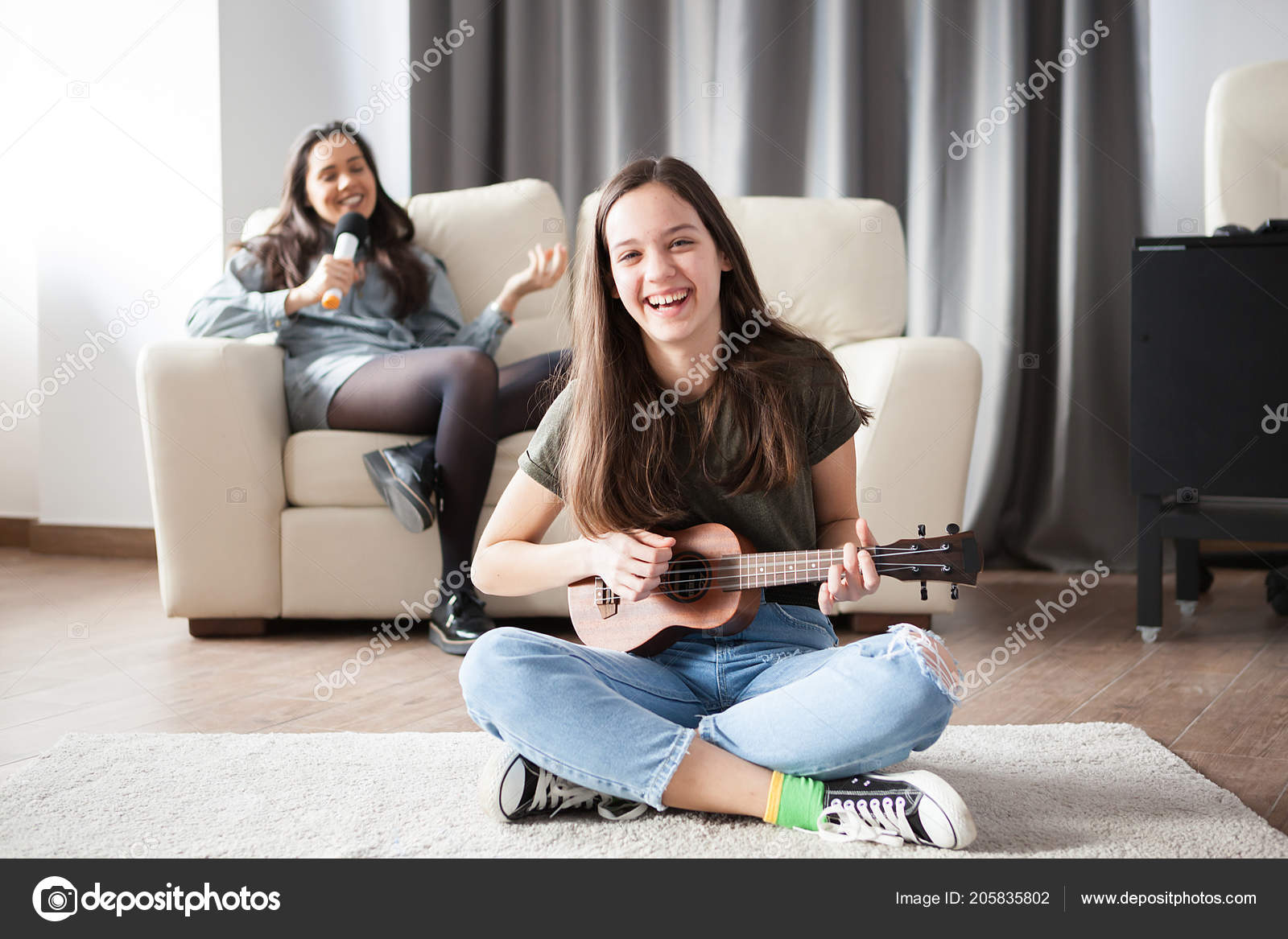 Two sisters, the younger one is playing a small guitar in front at the ...