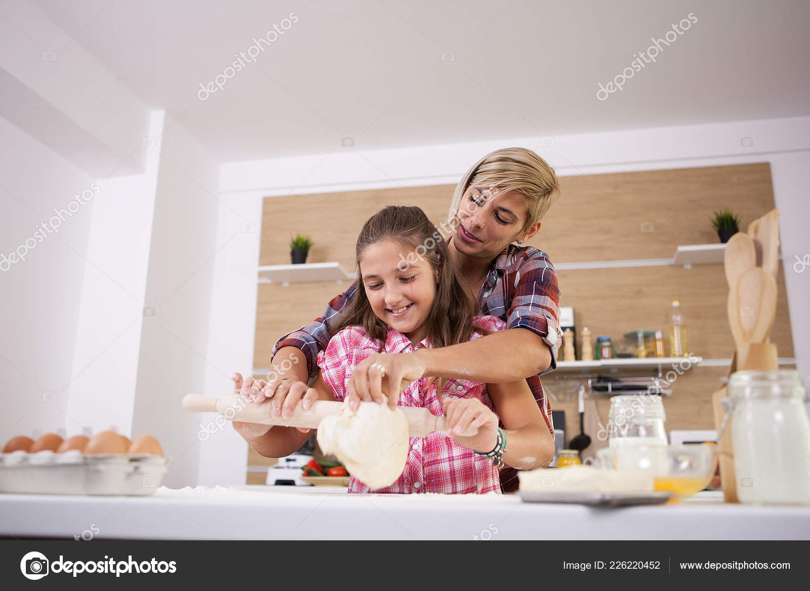 Teenage girl and her mother smiling while they are cooking together ...