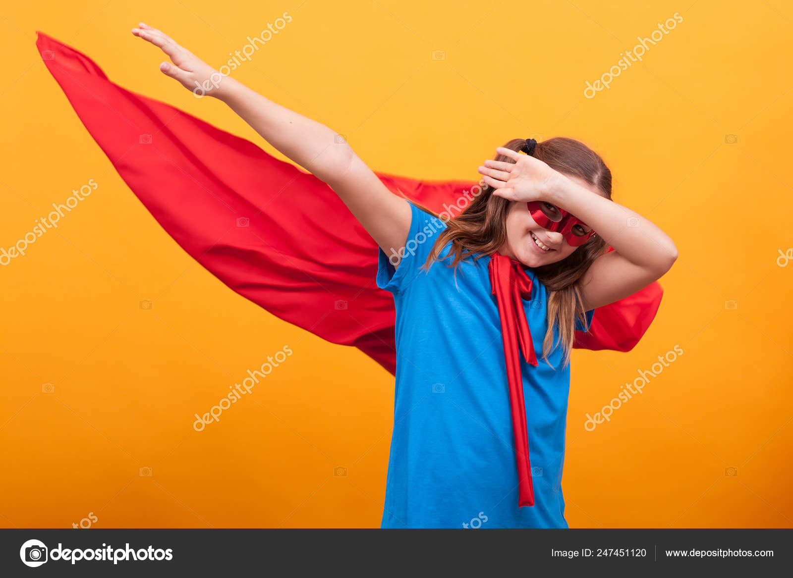 Little girl in red cape plays superhero in studio over yellow ...