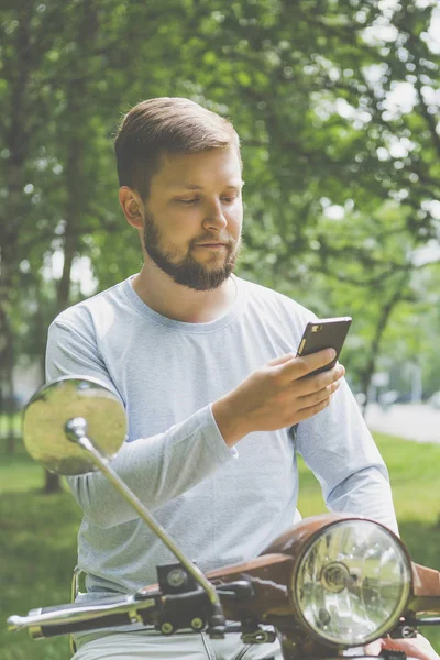 young man with phone riding a vintage scooter in the park - Stock Image ...