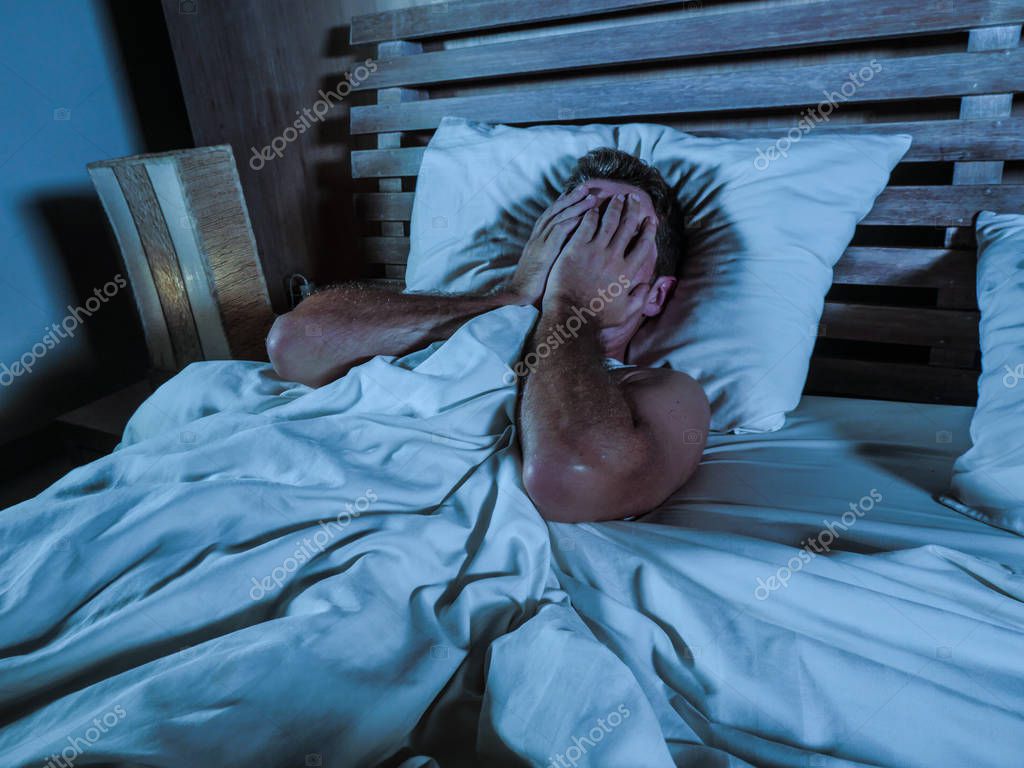 joven hombre triste y desesperado acostado en la cama llorando deprimido cubriendo la cara con ...