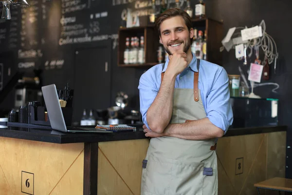 Shot of happy young bar owner standing near the counter and looking at ...