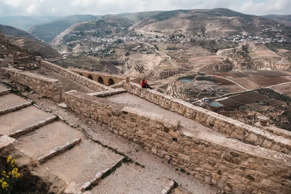 Ancient stone walls and resting female tourist in landscape of desert ...
