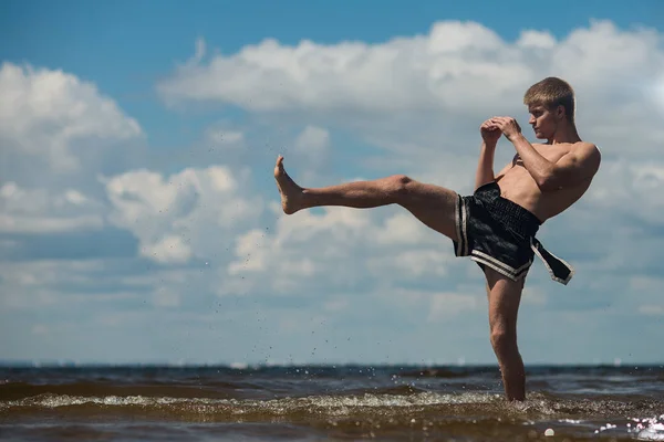 Kickboxer kicks in the open air in summer against the sea. Combat sport ...