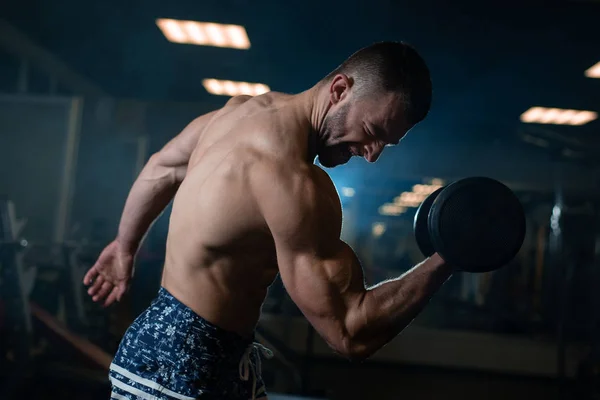 Handsome young muscular man exercising with dumbbells. Guy trains his ...