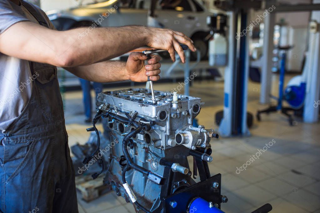 Mecánico con una herramienta en sus manos reparando el motor de la máquina. El proceso de ...