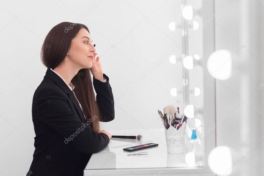 una chica, un maquillador, con el pelo largo y oscuro en un traje de negocios, se sienta en una ...