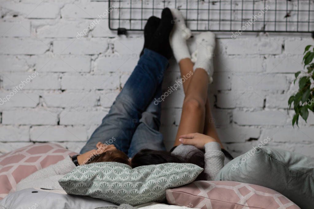 Un joven y su novia tumbados en la cama, tirando sus pies en la pared de ladrillo blanco 2023