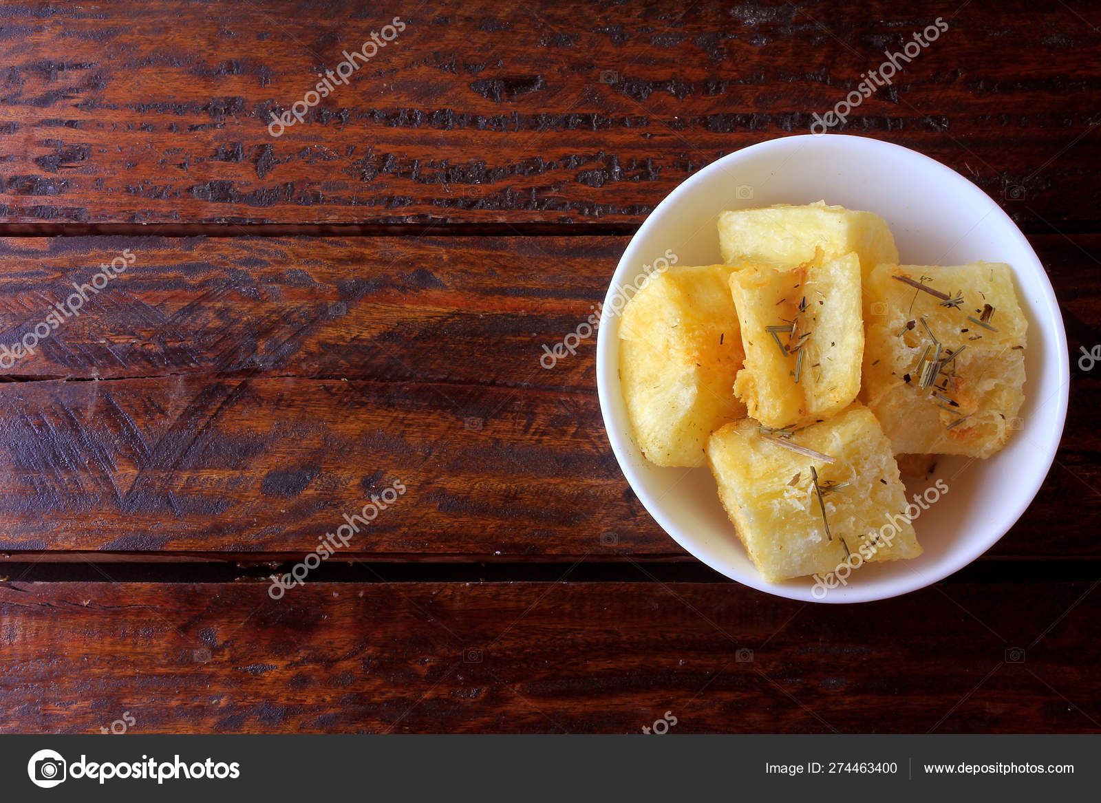 Boiled and fried cassava (mandioca) in ceramic bowl on rustic wooden ...