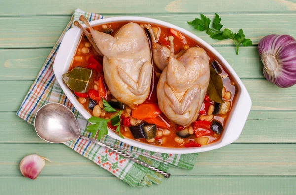 Stewed poultry with vegetables and beans in a dish on a green wooden ...