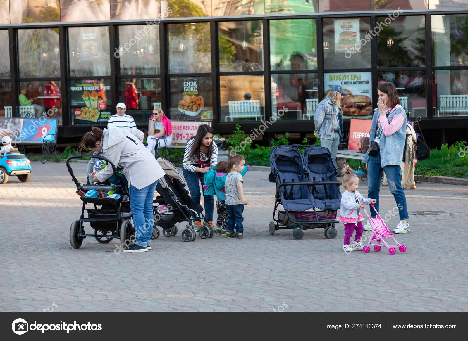 Young mom girls with strollers and small children are walking in ...