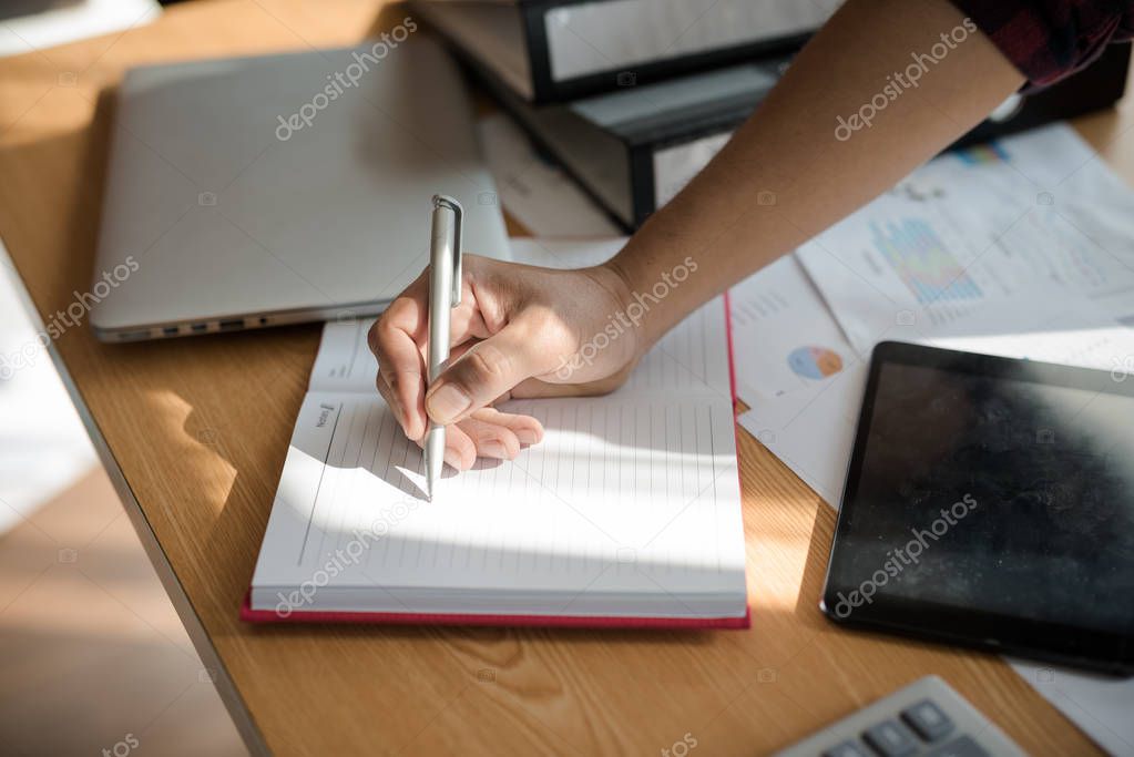 Mano de hombres de negocios sosteniendo la pluma mientras escriben notas en el libro durante la ...