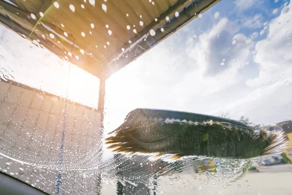 Young worker drying cars windshield at car wash. Cleaning window ...