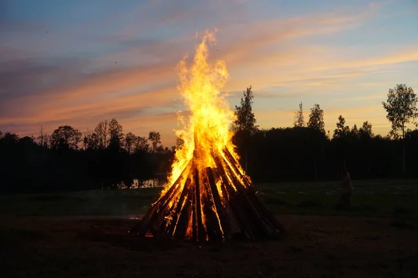 A large bonfire burns at midsummer night, with the sun setting in the ...