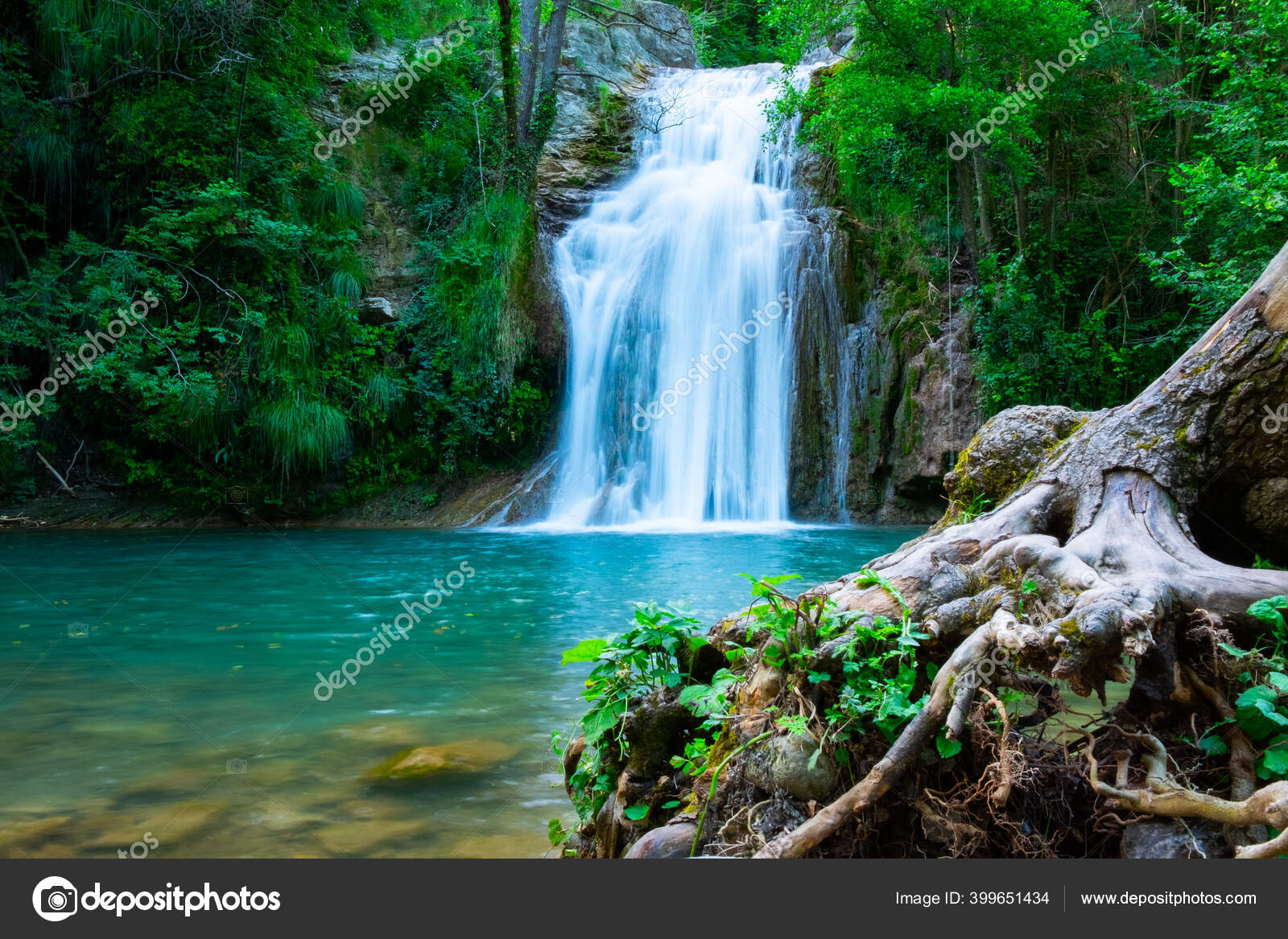 A large beautiful waterfall in a forest with blue water and a tree ...