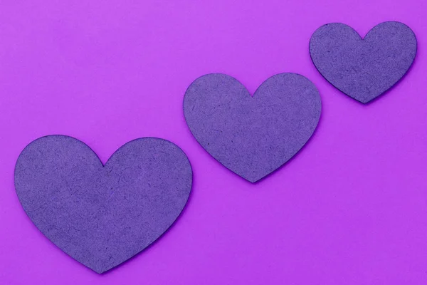 Three hearts of different sizes of cherry color on a purple background ...