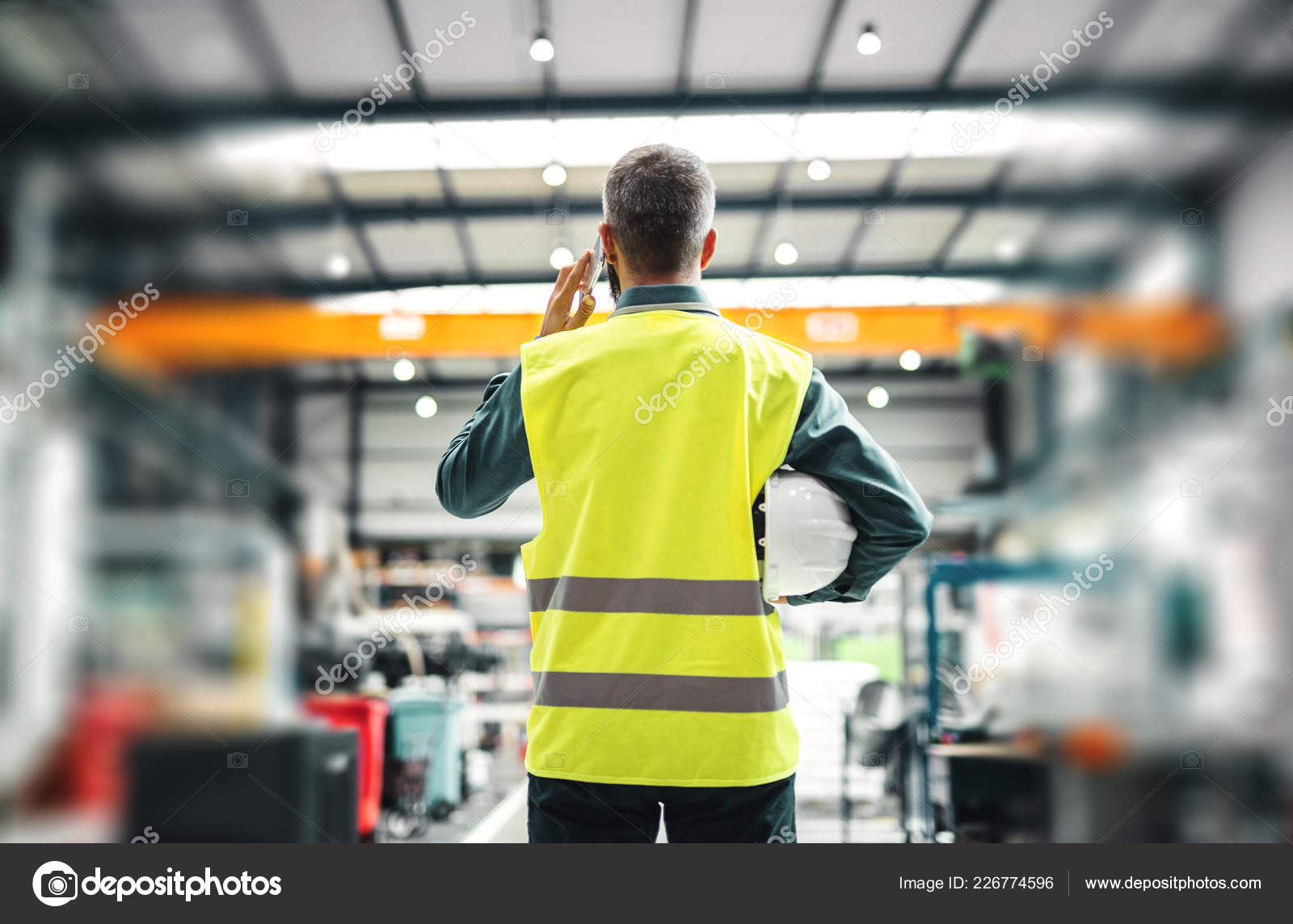 A rear view of an industrial man engineer with smartphone in a factory ...
