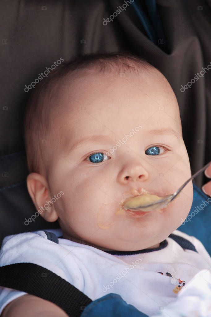 Lindo niño caucásico alimentado con cuchara pequeña en silla de bebé ...