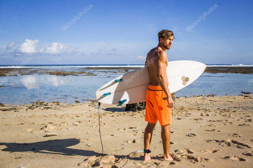 joven con tabla de surf en la playa de arena cerca del océano 2022