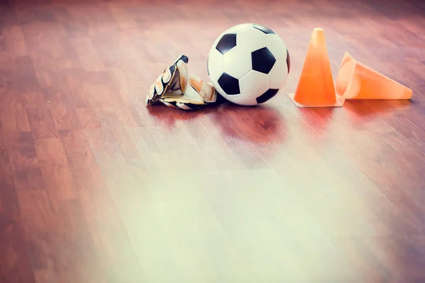 Soccer ball , gloves and marker cones are on wooden futsal floor ...