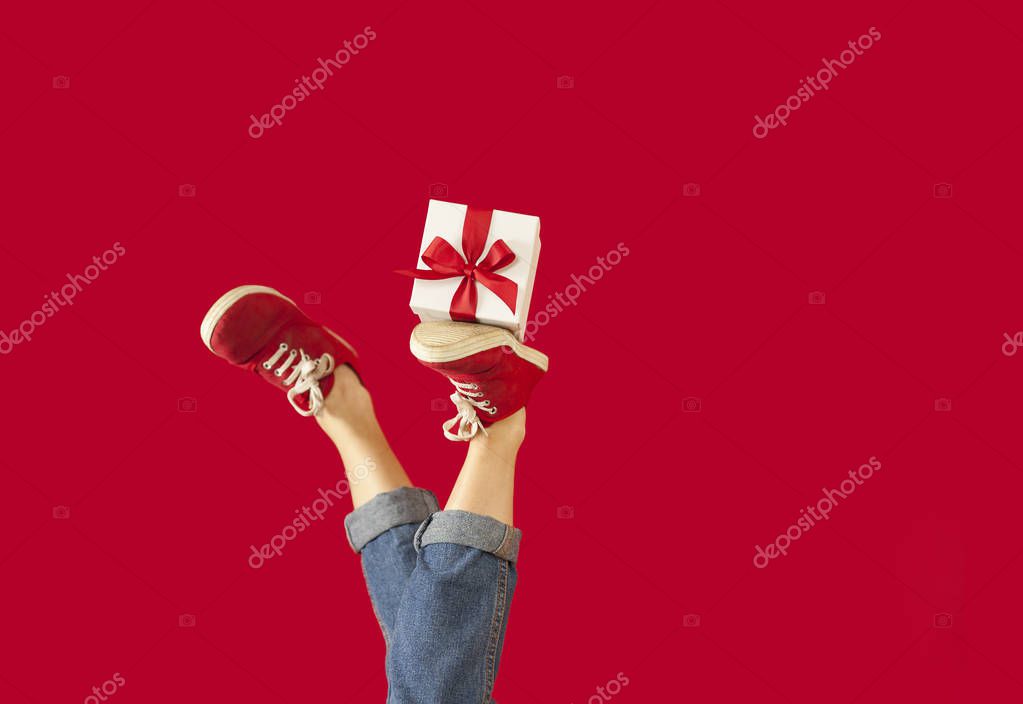 pies con un regalo para las vacaciones sobre un fondo rojo aislado, una chica con un regalo ...