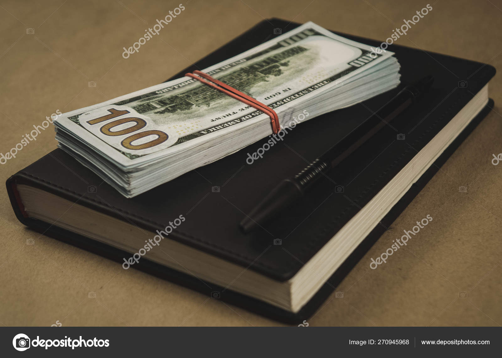 A black notebook , a pen and dollar cash banknotes on wooden background ...
