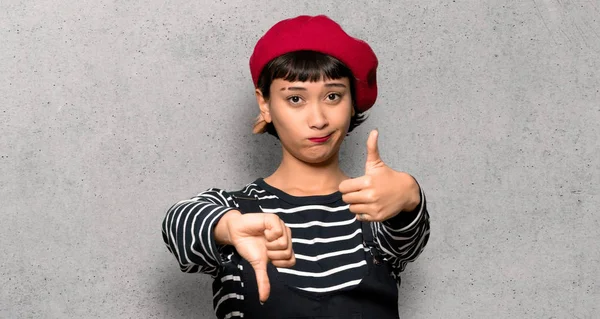 Young woman with beret making good-bad sign. Undecided between yes or ...