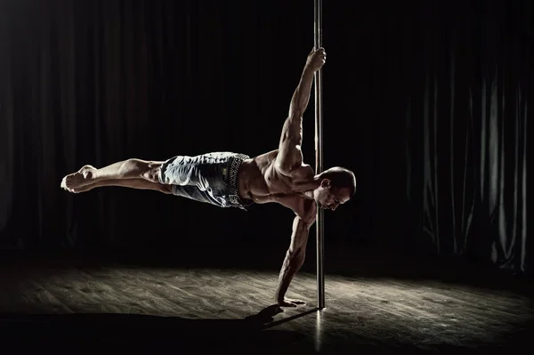 Pole dance male athlete. Strong and muscular guy executes a trick. Pole ...