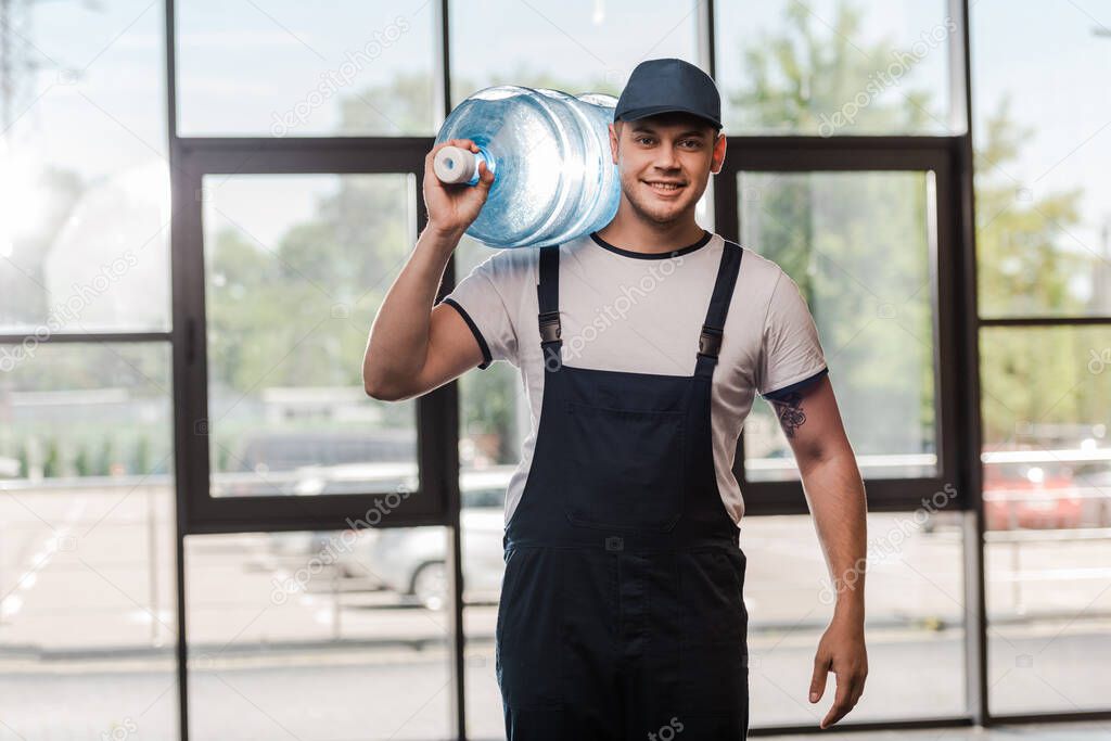 alegre repartidor hombre en gorra y uniforme sosteniendo galón de agua ...