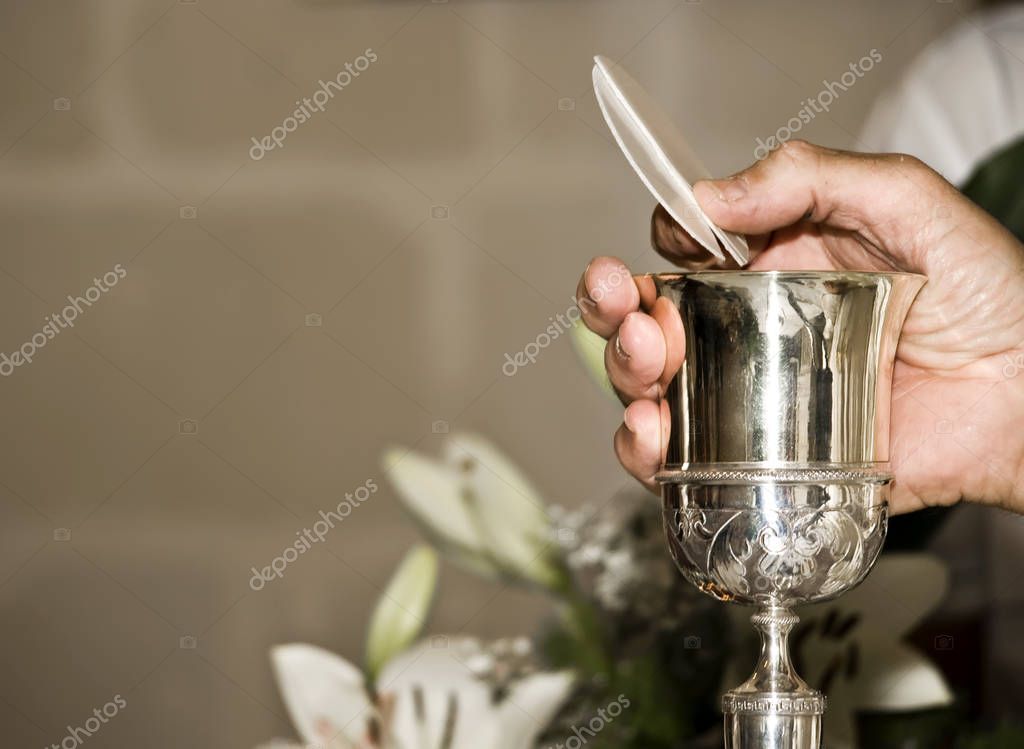 Mano del sacerdote sosteniendo pan santo y cáliz durante la Misa 2023