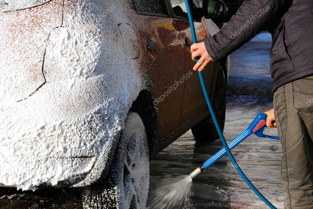 El hombre lava su coche naranja en el lavado de autos. Limpieza con ...