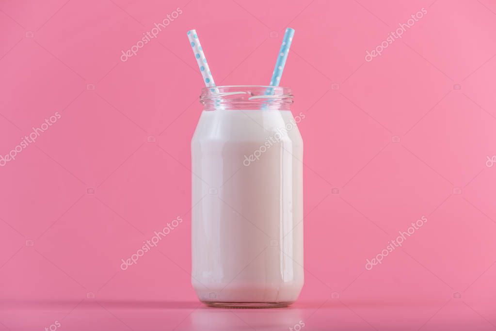 Botella de vidrio de leche fresca con dos pajitas sobre fondo rosa ...