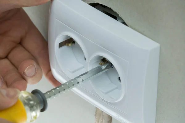 A man installs an electrical outlet in the wall. Close up of technician ...