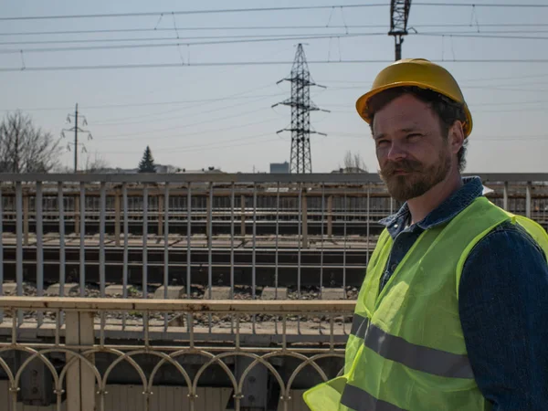 A man with a beard and mustache in a helmet stands on a bridge near the ...
